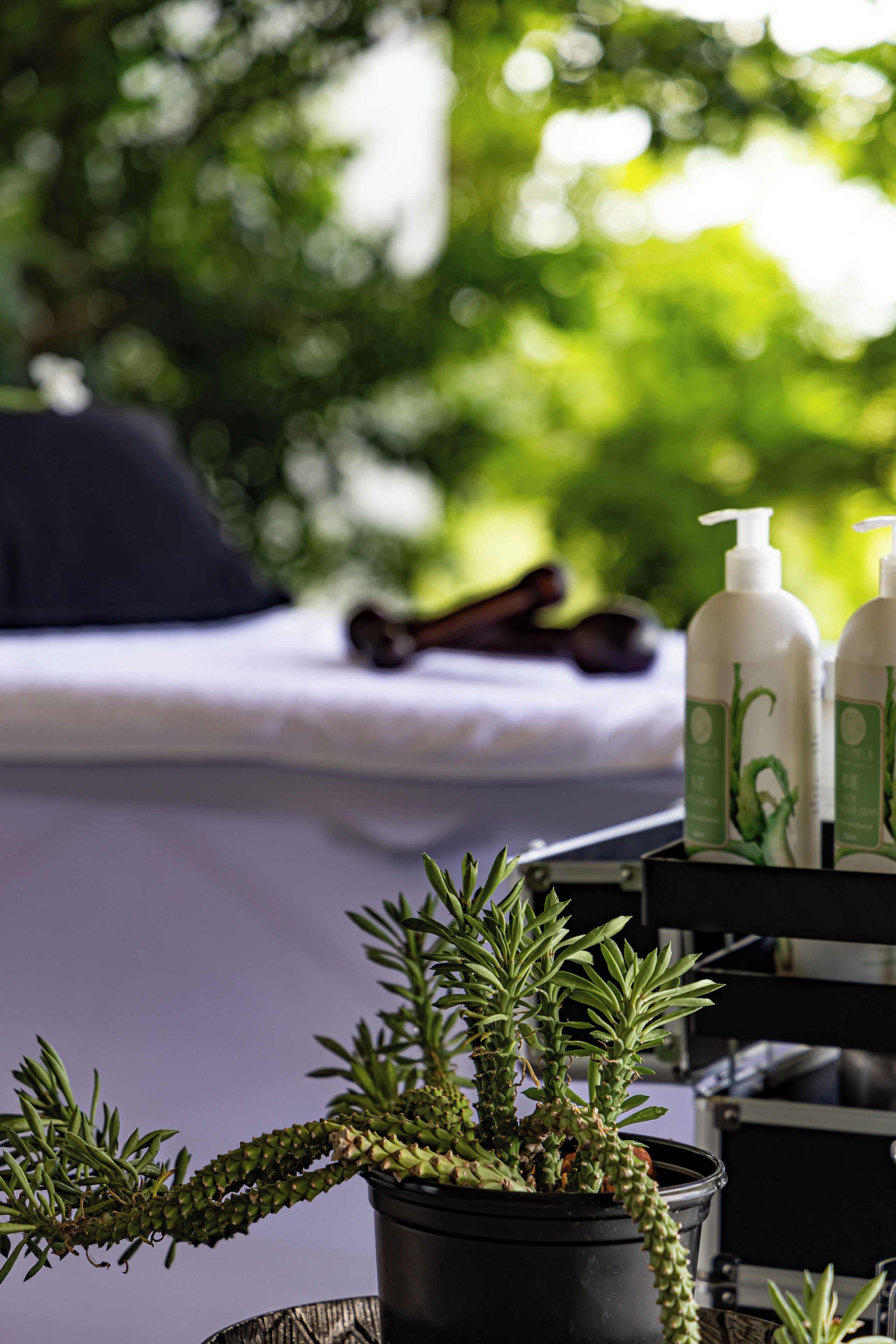 Uma cama com lençol branco, um par de óculos de sol e duas embalagens de loção em cima de uma mesa.