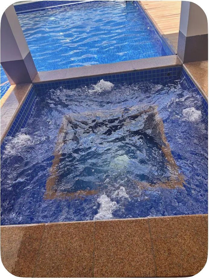 Piscina com área de hidromassagem retangular no centro, rodeada por um deck revestido de azulejos.