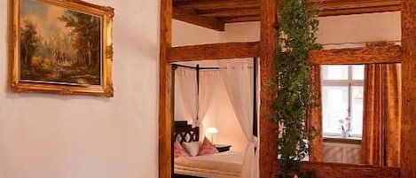 Quarto com teto de madeira, um lustre, sofá de couro preto, mesa de centro de vidro e uma cama com dossel.