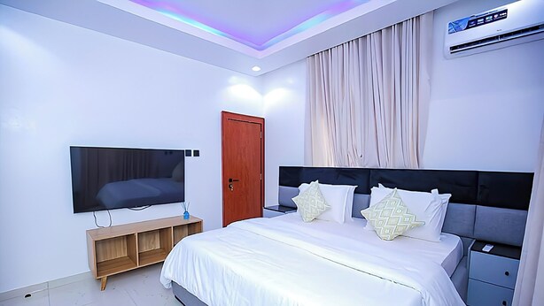Quarto moderno com uma cama grande, televisão, mesinha de cabeceira de madeira e ar condicionado.