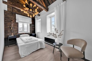 Quarto com teto de madeira, uma cama, uma cadeira, mesa de cabeceira e uma janela.