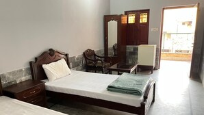 Quarto de hotel com duas camas de solteiro, um guarda-roupa de madeira, um espelho e uma pequena mesa.