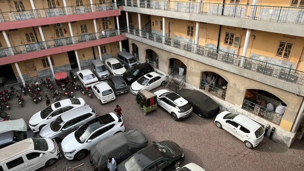 Uma estrutura de estacionamento com vários andares, diversos carros e um tuk-tuk.