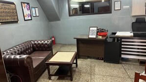 Quarto com sofá de couro, mesa de centro de madeira, escrivaninha com computador e espelho na parede.