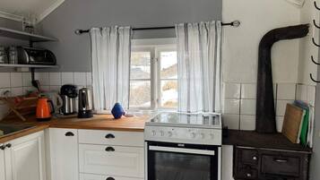 Uma cozinha com armários brancos, fogão, cafeteira e janela com cortinas.