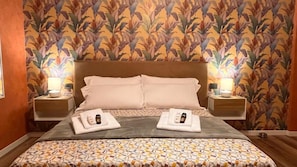 Quarto de hotel com uma cama grande, duas mesas de cabeceira com luminárias e um padrão floral no papel de parede.