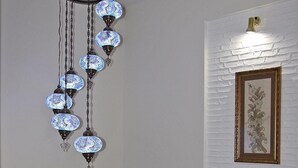 Uma escadaria com grades de metal elaboradas, um candelabro com luzes azuladas e um jarro decorativo dourado.
