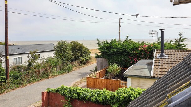 Um bairro residencial com rua pavimentada, cerca de madeira e vista para o mar.