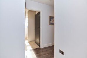Um corredor com piso de madeira escura, uma porta branca e um quadro na parede.