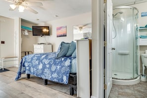 Quarto com cama, televisão, secretária e chuveiro.