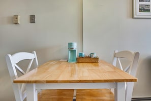 Uma mesa de madeira com cadeiras, uma garrafa de água azul-turquesa e um cesto com copos.
