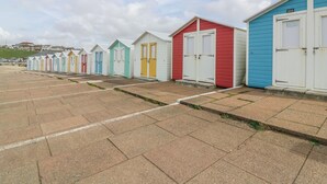 Uma fileira de cabanas de praia com portas e janelas brancas, numeradas em sequência, e um calçadão pavimentado na frente.