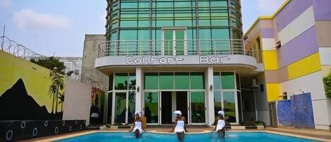 Hotel com área de piscina, design moderno com grandes janelas e um bar chamado "Confort Bar".