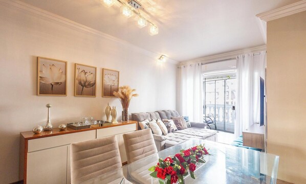 Uma sala de estar moderna com uma mesa de jantar de vidro, um sofá e um vaso decorativo com flores.