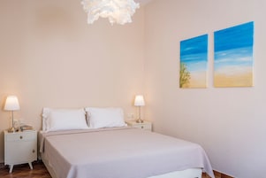 Quarto com cama, duas mesas de cabeceira, duas luminárias de parede e duas pinturas.
