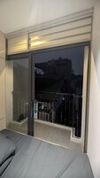 Quarto com cama, porta de vidro deslizante para uma varanda e vista de edifícios.