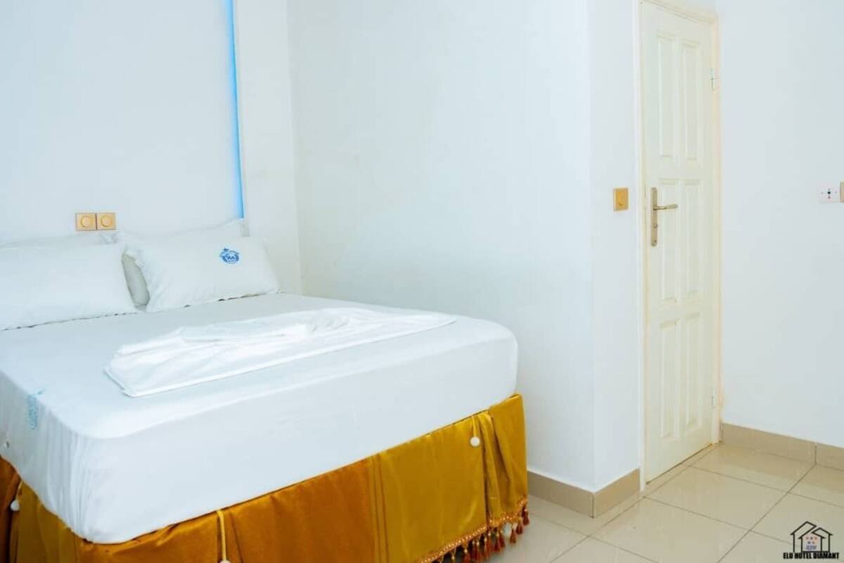 Quarto de hotel com uma cama, uma porta e um interruptor de luz na parede.