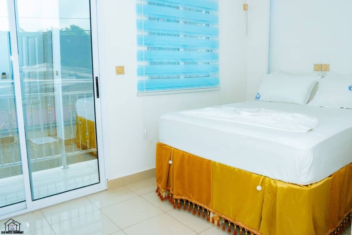 Quarto de hotel com uma cama, uma porta de vidro deslizante e uma janela com persianas.