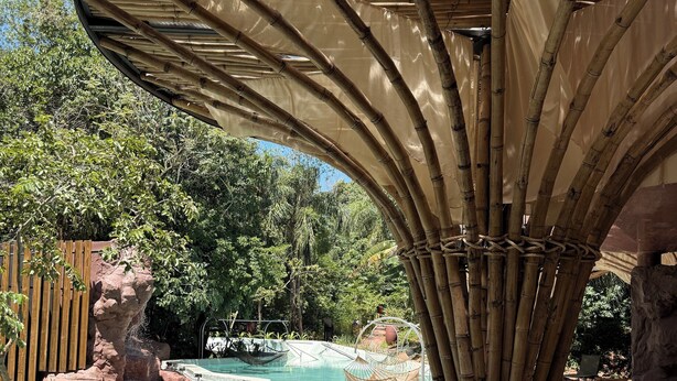 Uma área de piscina com estrutura de bambu sobre a cabeça, rodeada por vegetação e paisagem rochosa.