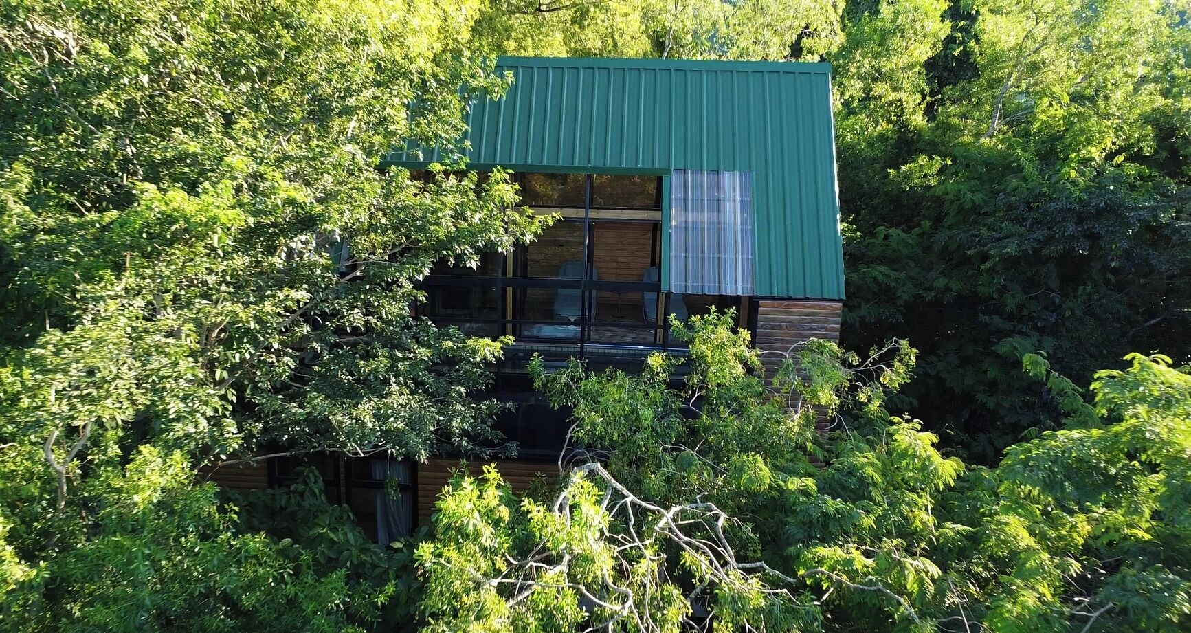 Uma cabana com telhado verde, rodeada por uma floresta densa.