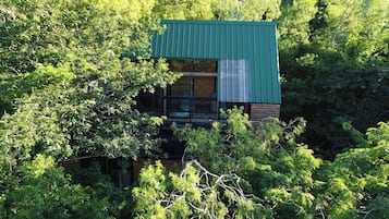 Uma cabana com telhado verde, rodeada por uma floresta densa.
