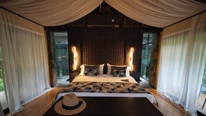 Quarto com cama, abajures, chapéu sobre uma mesa e vista através de uma porta de vidro.