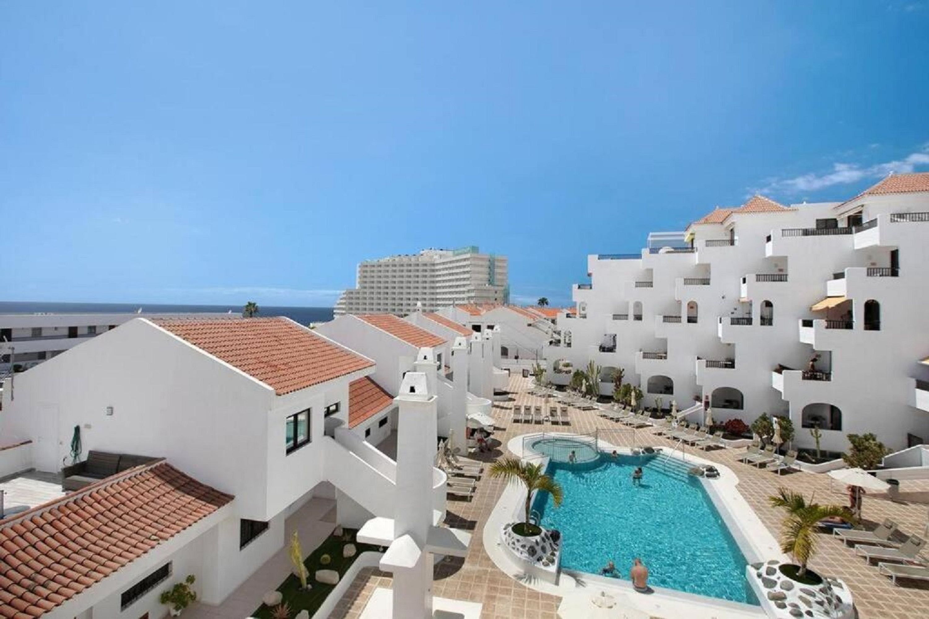 Um resort com piscina, edifícios brancos e vista para o oceano.