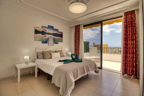 Quarto com cama, mesa de cabeceira, pintura e vista para o exterior.