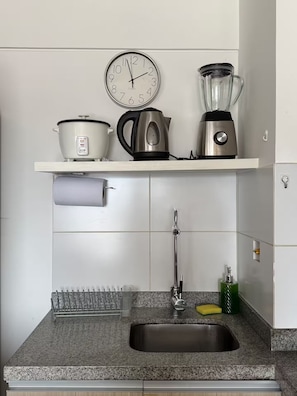 Cozinha com bancada de granito, pia, fogão, relógio, chaleira, liquidificador e escorredor de louça.