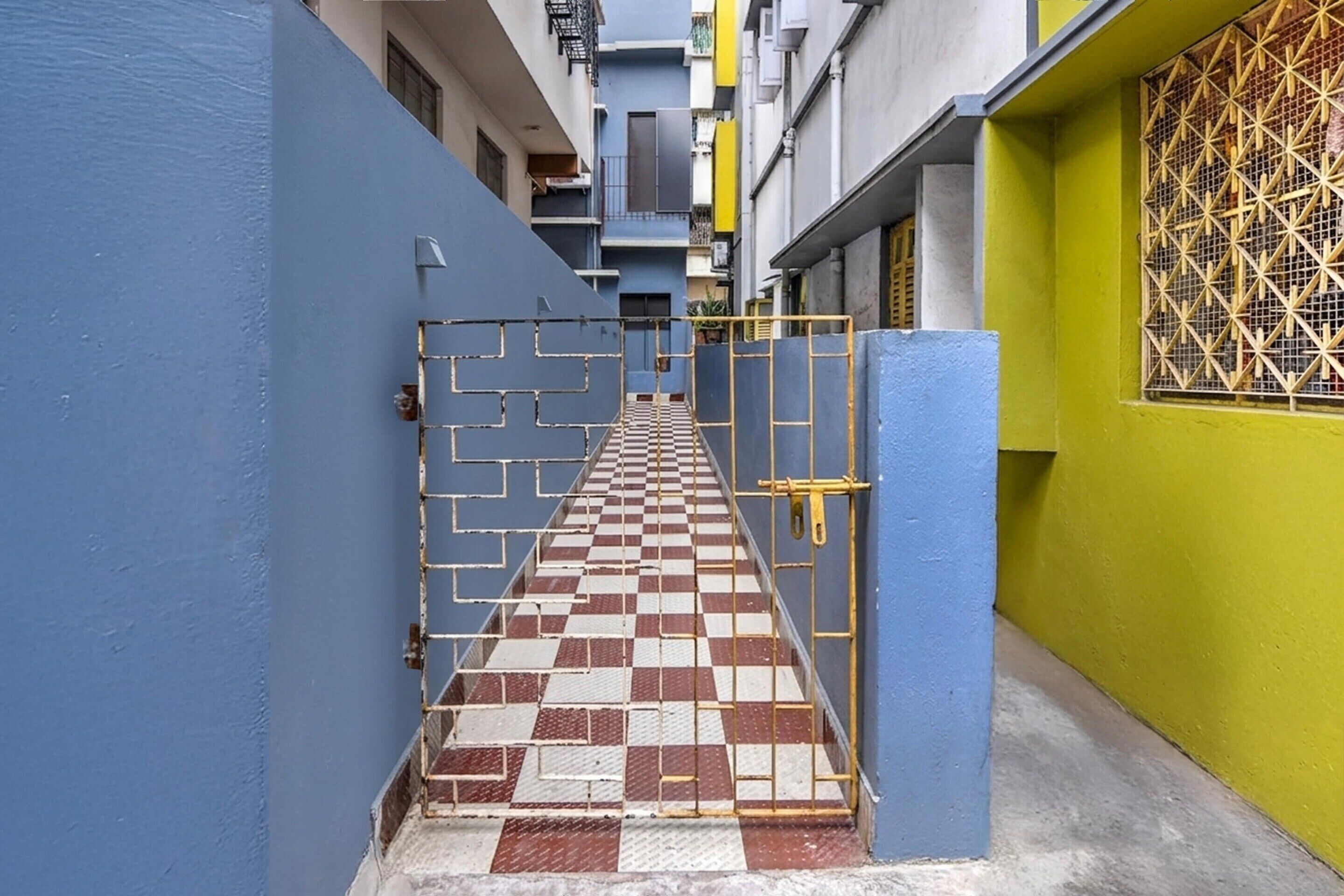 Um beco estreito com chão de ladrilhos xadrez, que leva a um portão.