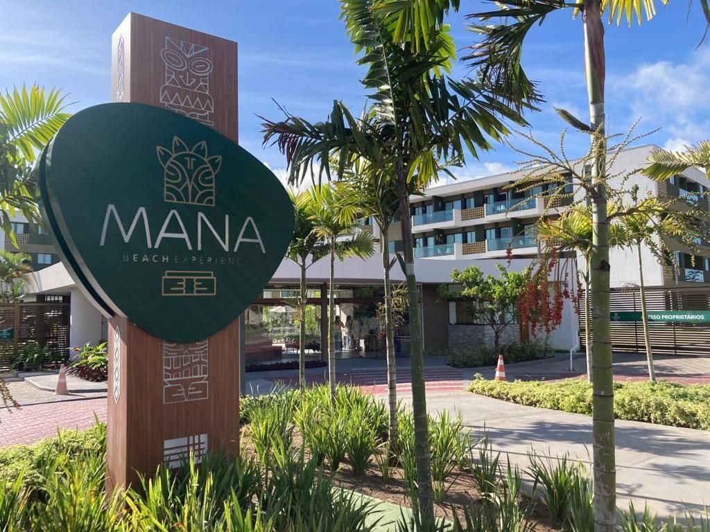 Placa de 'MANA Beach Experience' com um edifício moderno ao fundo.