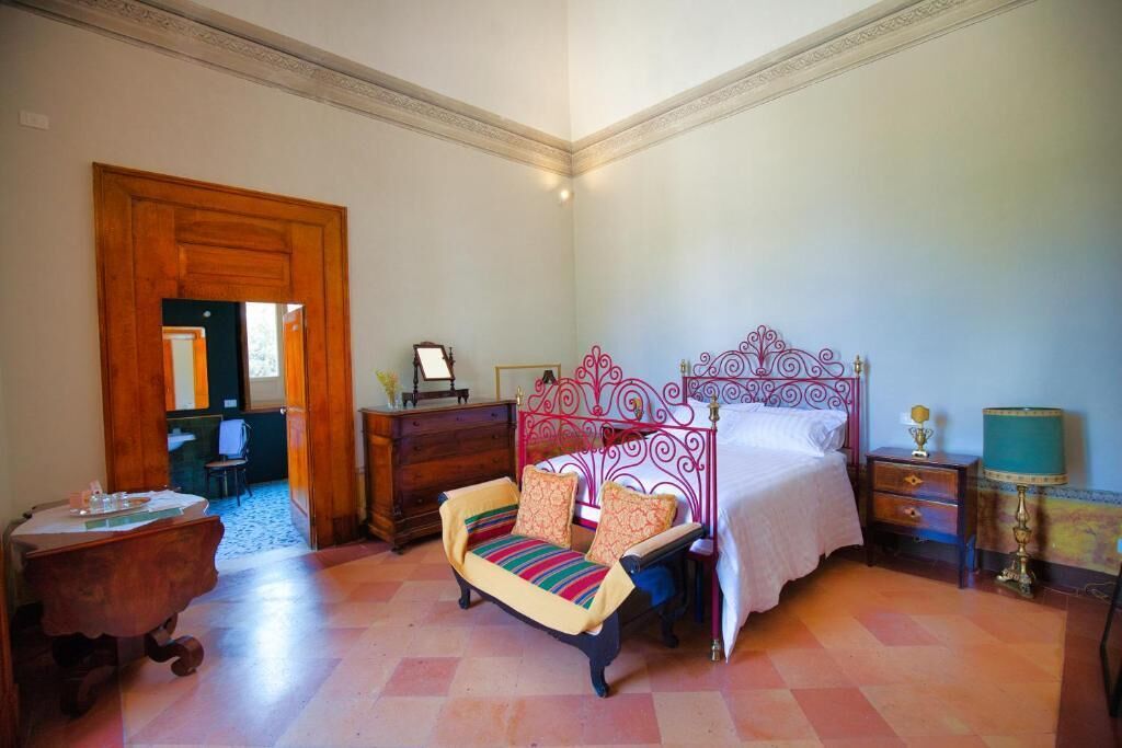 Quarto com cama grande, cómoda de madeira, cadeira e mesa pequena.