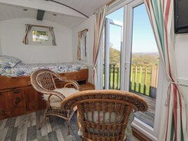 Um quarto aconchegante com uma cama, cadeiras de vime e uma grande janela com vista para uma paisagem verde.