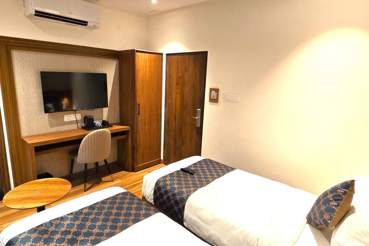 Quarto de hotel com duas camas, uma escrivaninha com televisão e uma pequena mesa.