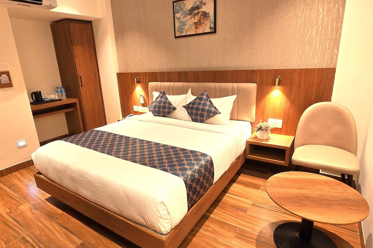 Quarto de hotel com uma cama grande, mesas de cabeceira, uma cadeira e uma pequena mesa redonda.