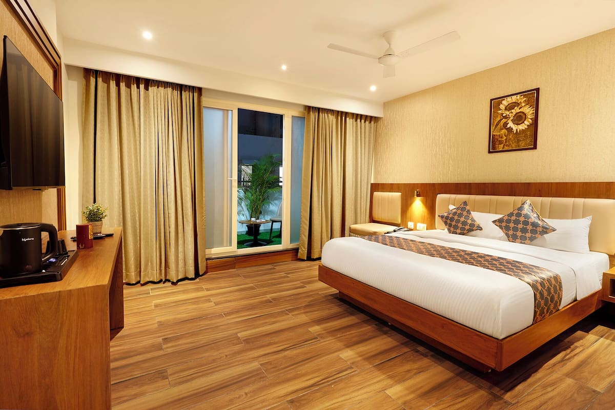 Quarto de hotel com cama, secretária com cafeteira, televisão e vista para o exterior.