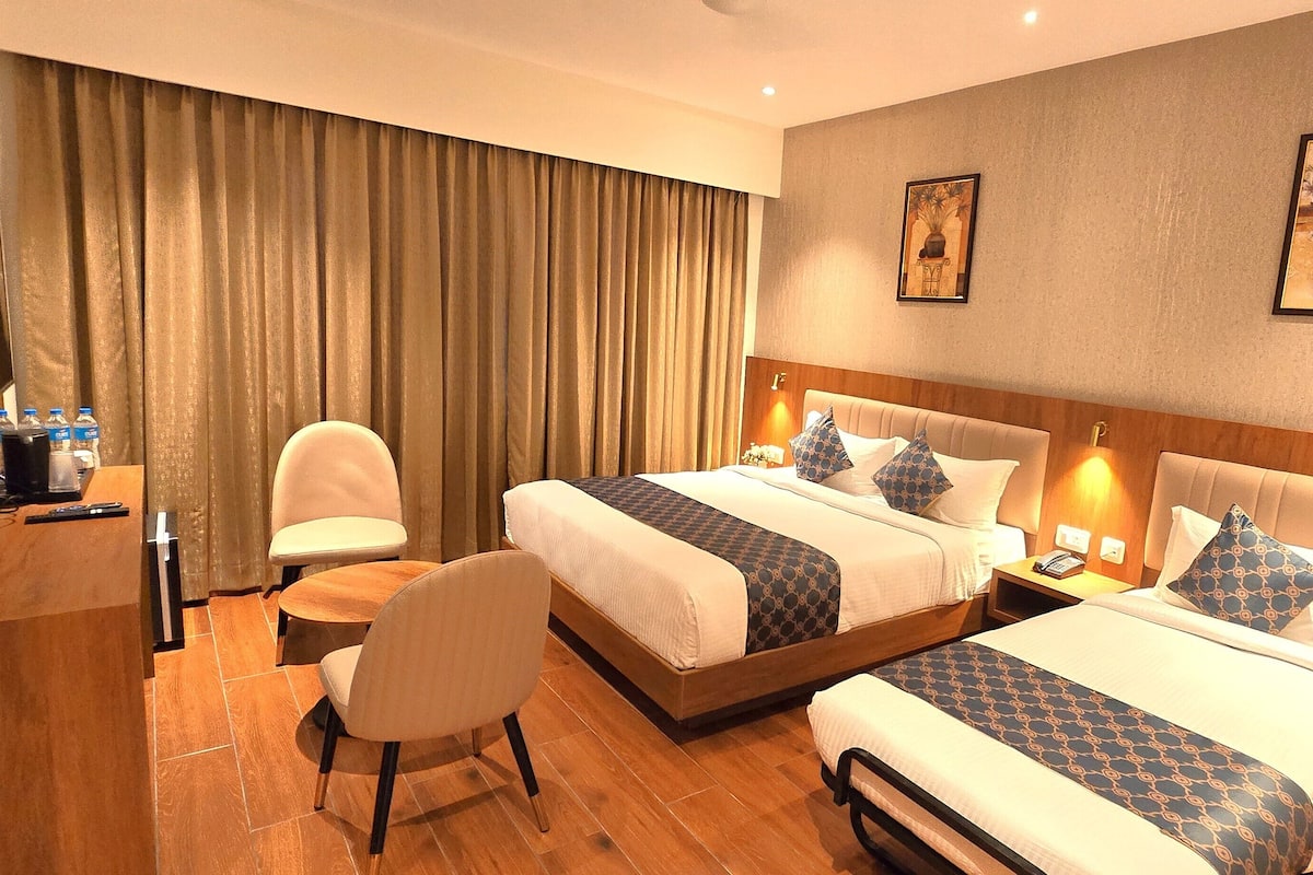 Quarto de hotel com duas camas, uma escrivaninha, uma cadeira e uma televisão.