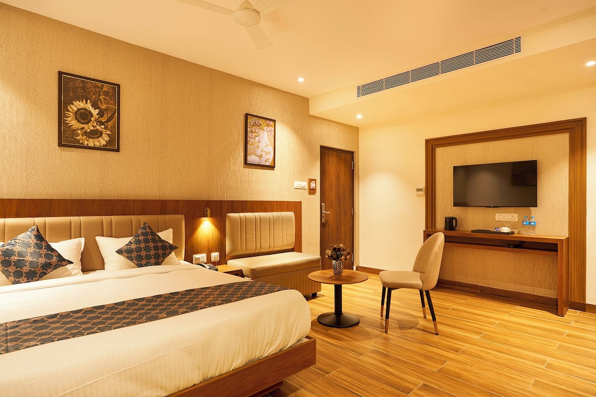 Quarto de hotel com uma cama grande, uma escrivaninha com televisão e uma cadeira.