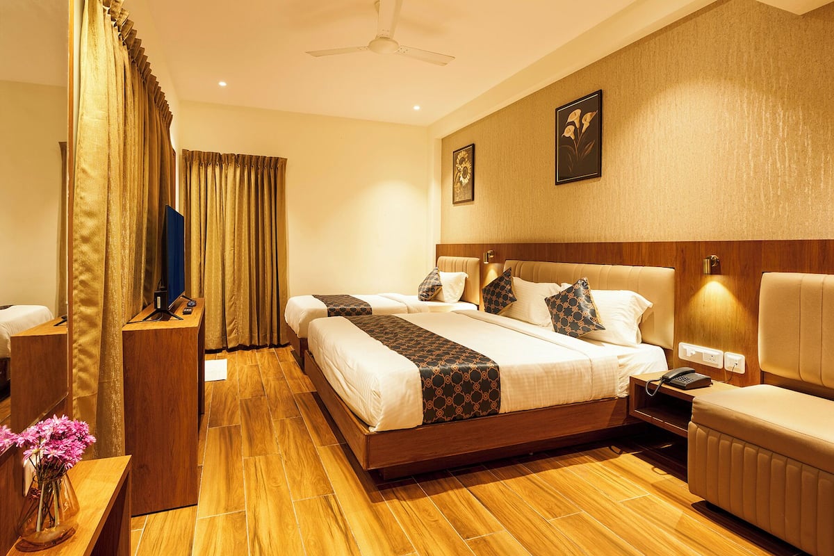 Quarto de hotel com uma cama grande, uma escrivaninha com computador, uma cadeira e uma mesinha de cabeceira.