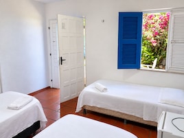 Quarto com duas camas, uma porta branca e janela com persianas azuis.