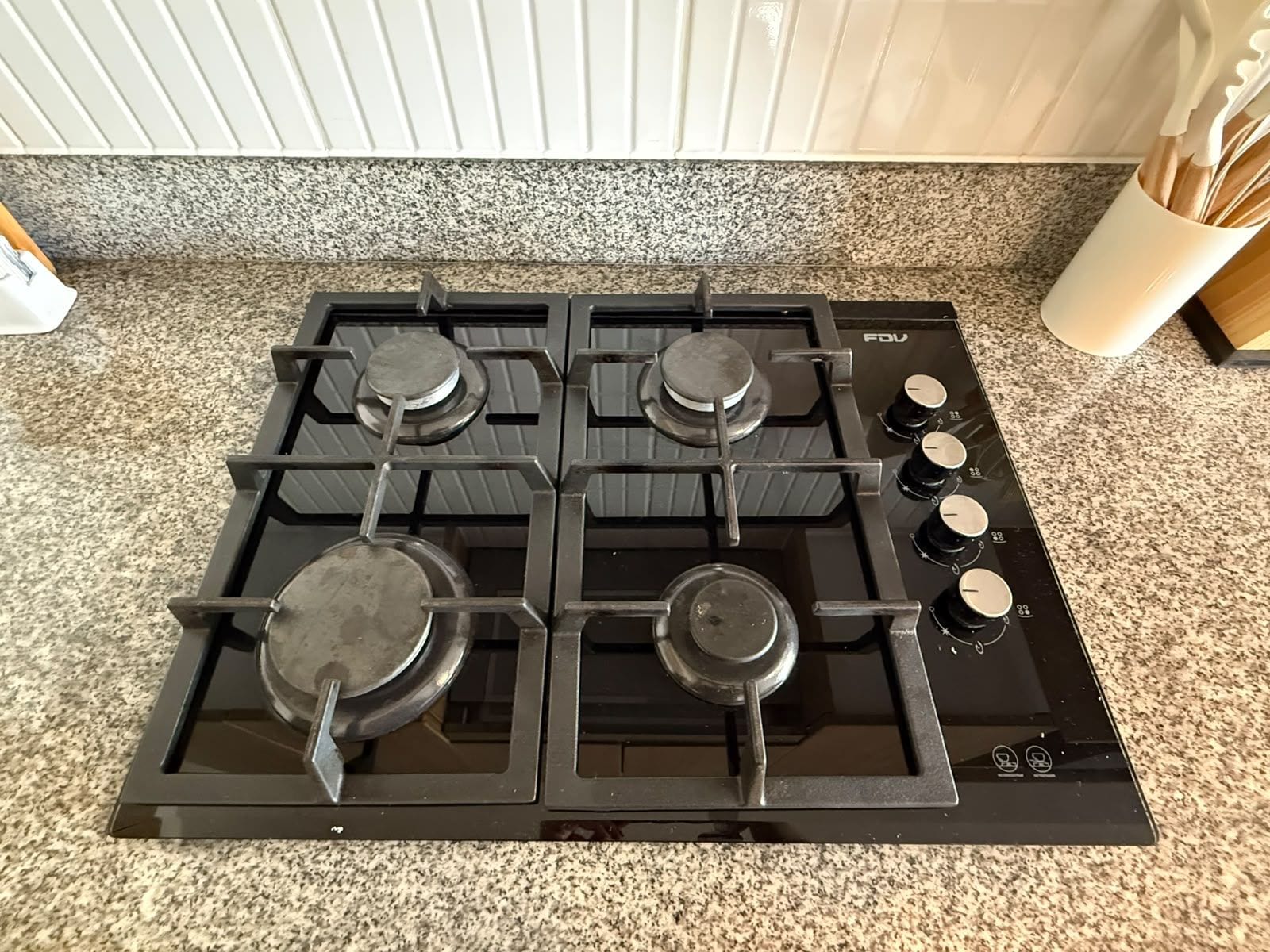 Cozinha com fogão a gás, bancada de granito e parede branca.