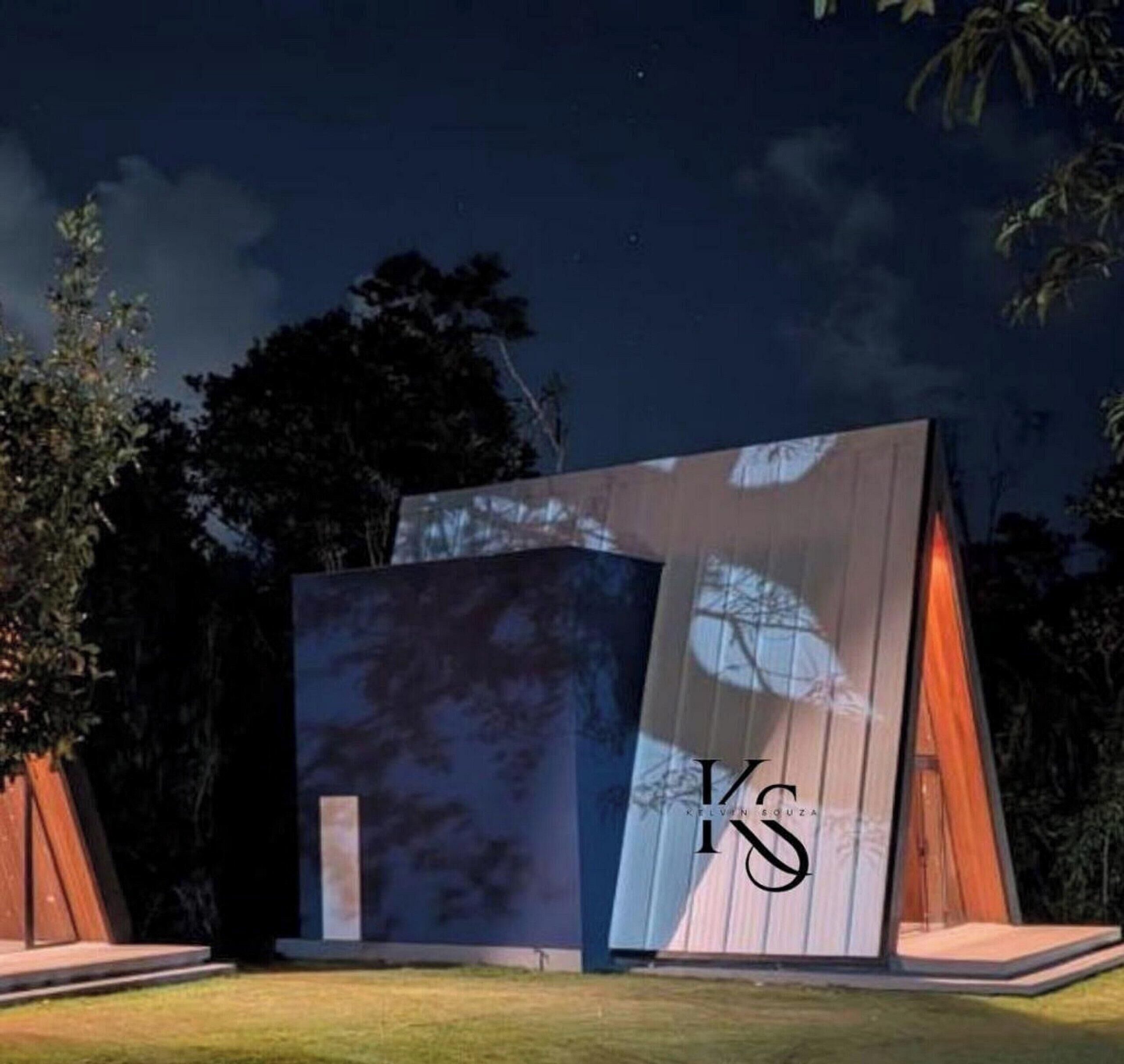 Um edifício moderno em formato triangular, com fachada de vidro, rodeado por árvores e um jardim bem cuidado.