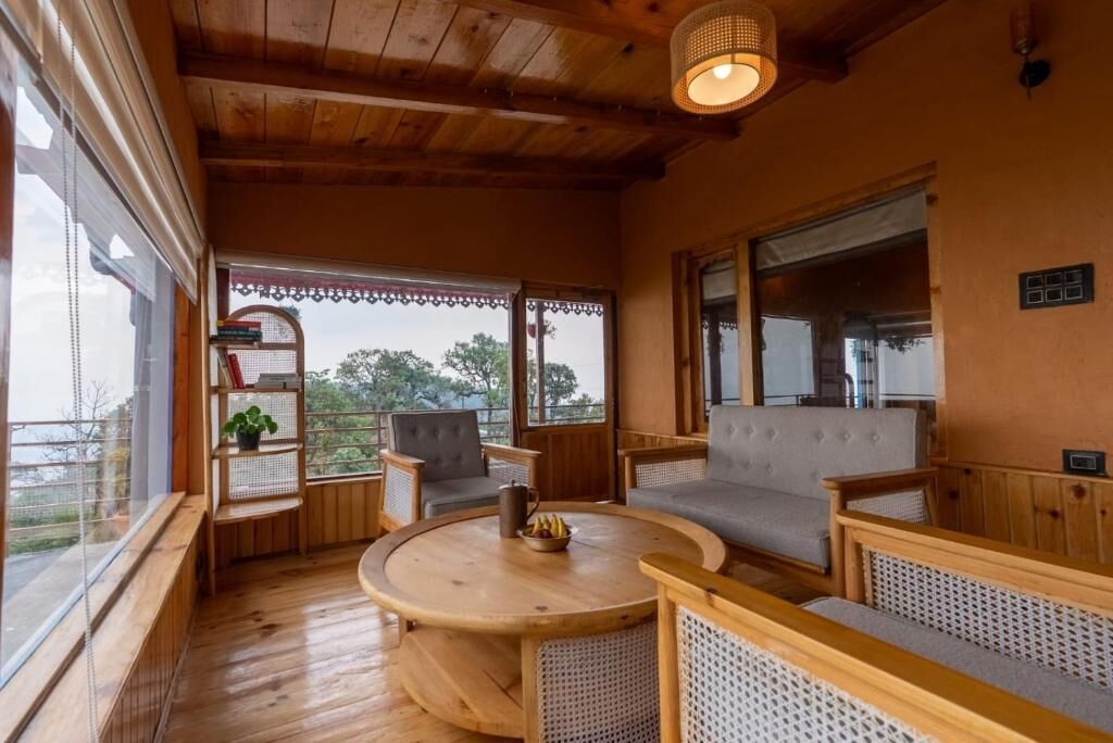 Um quarto acolhedor com uma mesa de madeira redonda, assentos estofados e uma grande janela com vista para o exterior.