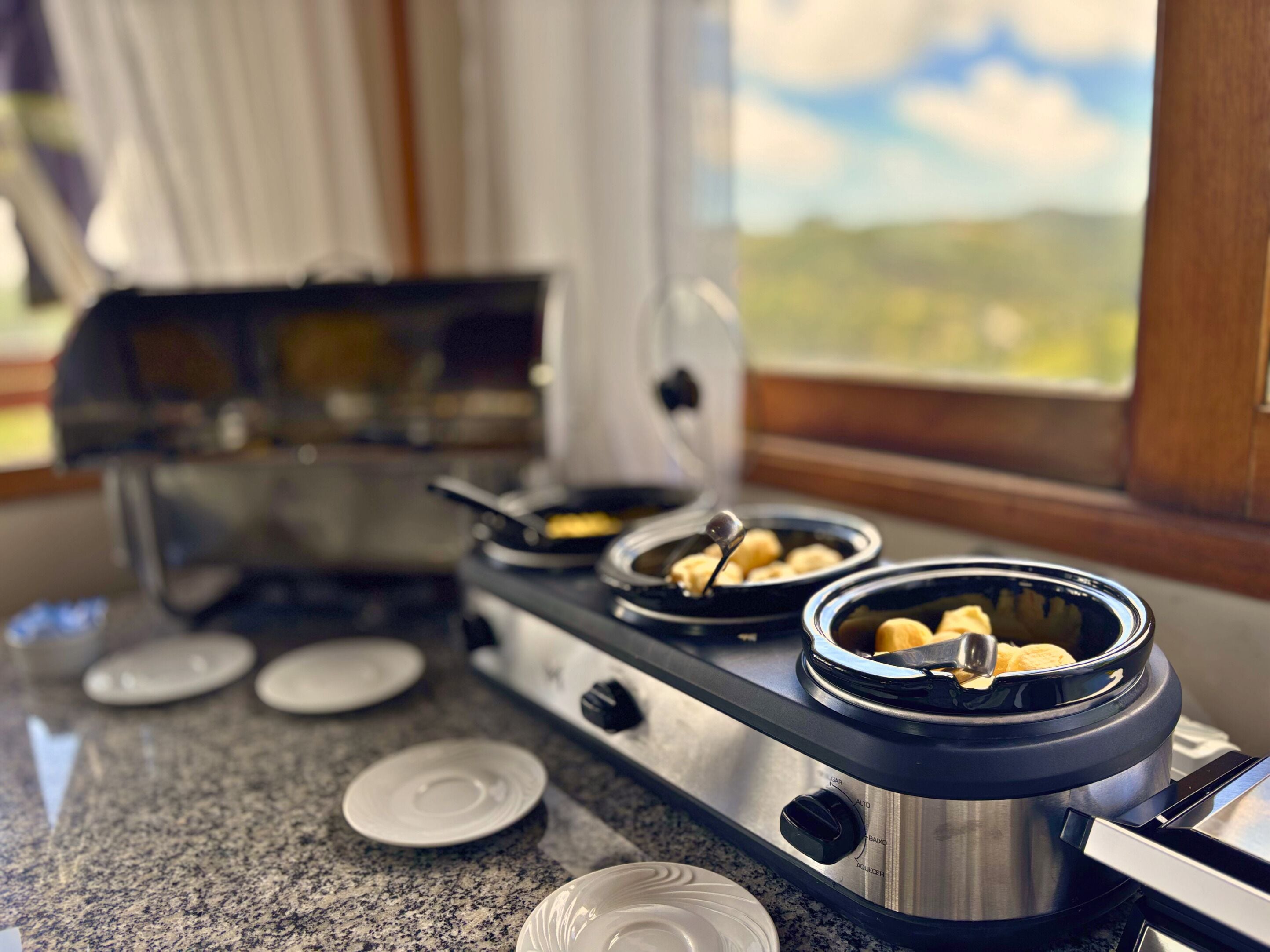 Cozinha com fogão a gás, duas frigideiras e janela com vista para o verde.