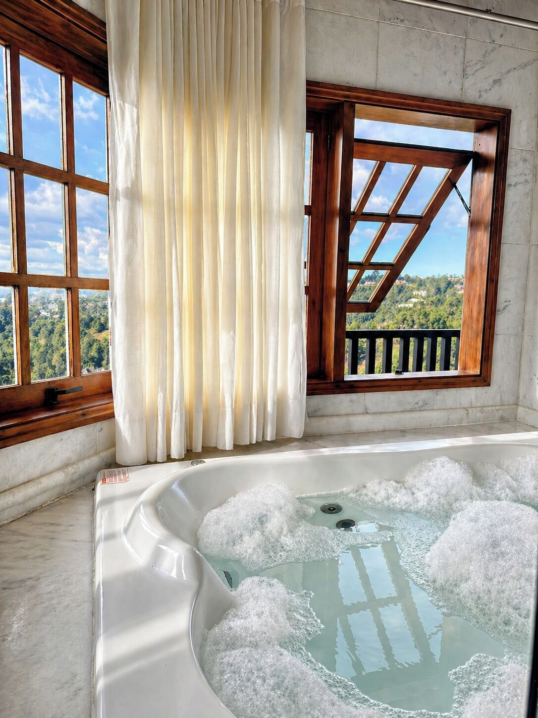 Quarto com banheira de hidromassagem, janelas amplas e vista para a paisagem.