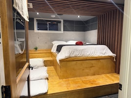Quarto pequeno com cama, uma janela e um banquinho de madeira.