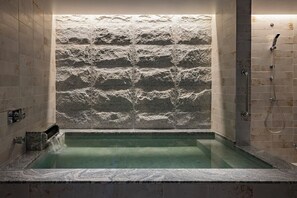 Uma área de spa com parede de pedra, uma banheira e um chuveiro.