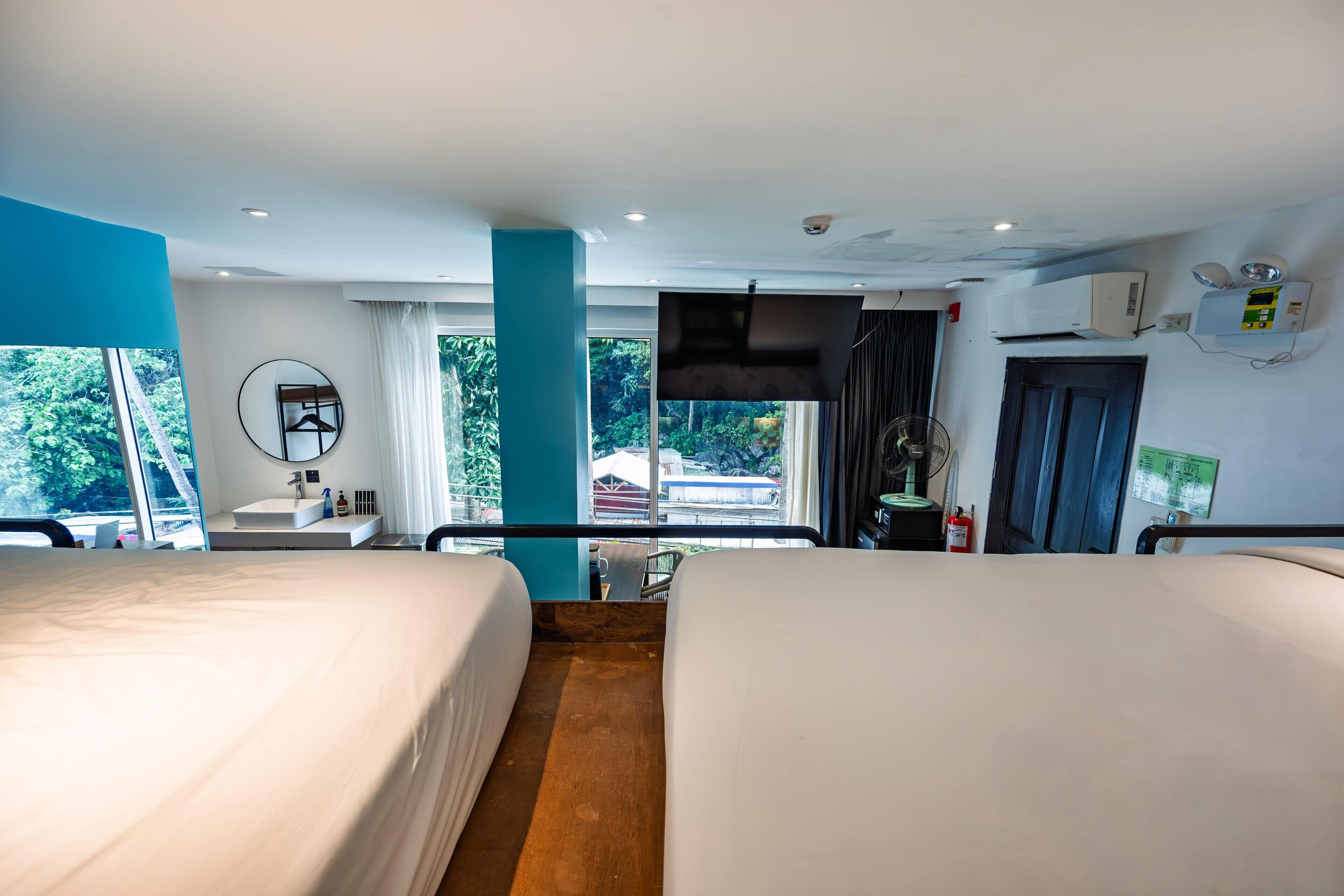 Quarto de hotel com duas camas, janela com vista, pia, espelho e ventoinha no teto.
