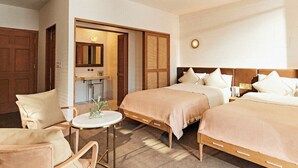 Quarto de hotel com duas camas, área de estar com uma mesa, um espelho e um ventilador de teto.