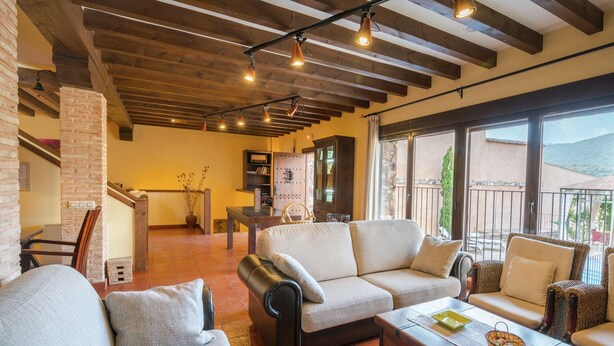 Uma sala de estar ampla com teto de madeira, um sofá, uma mesa de centro e vista para um pátio externo através de uma porta de vidro.